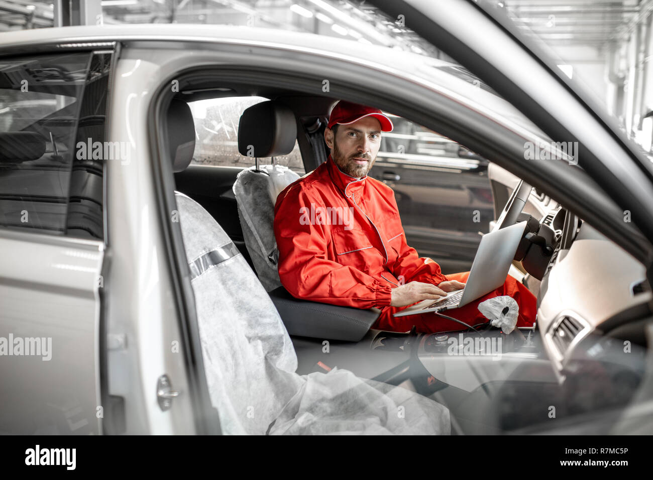 Auto mechanic in red uniform diagnosing car with computer sitting on ...
