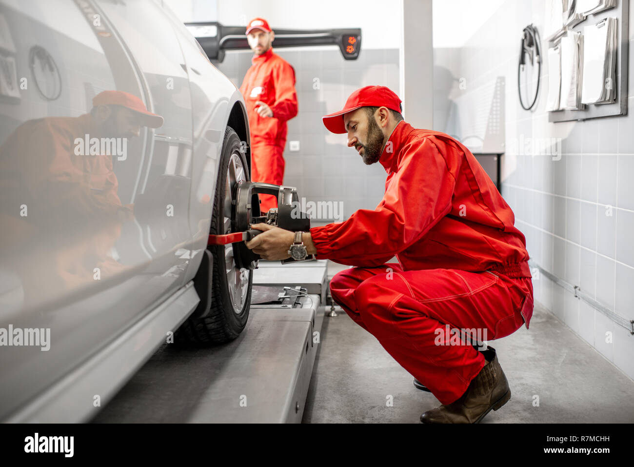 Handsome auto mechanic in red uniform fixing disk for wheel alignment ...