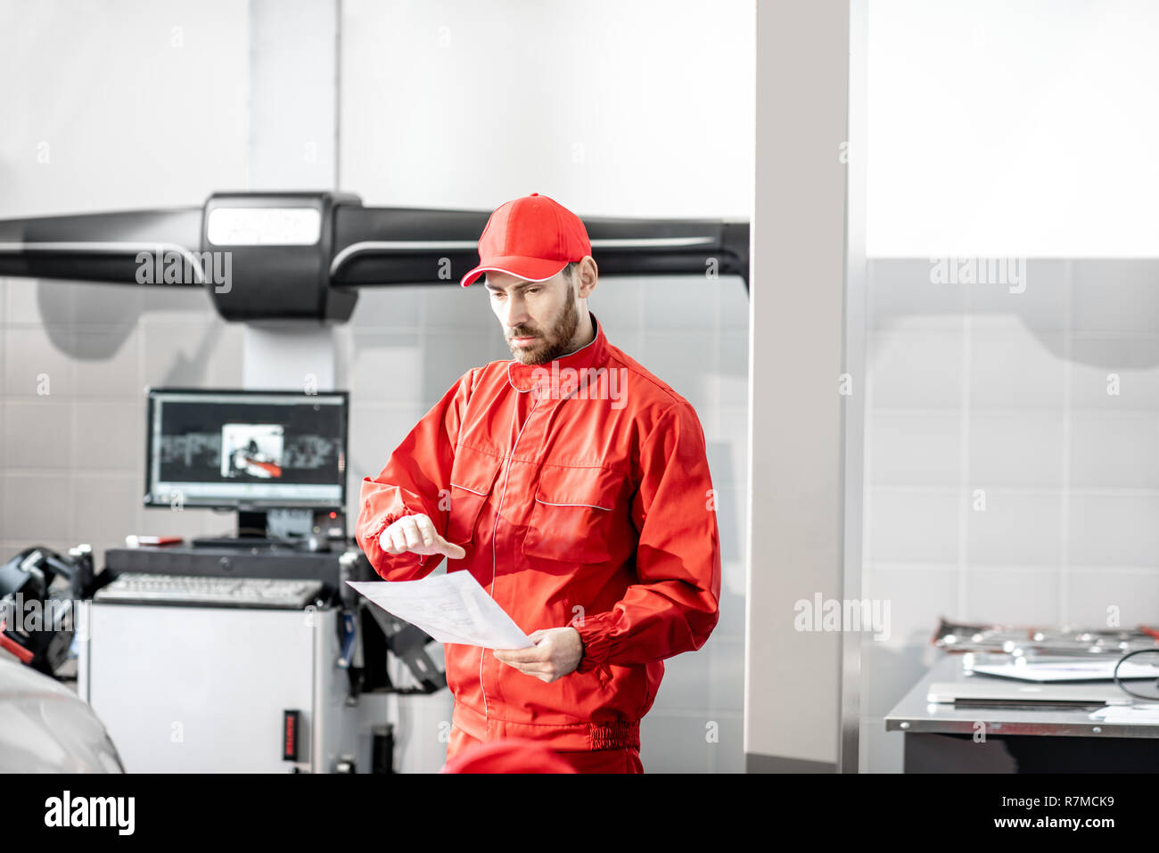 Auto mechanic in red uniform working with computer doing wheel ...