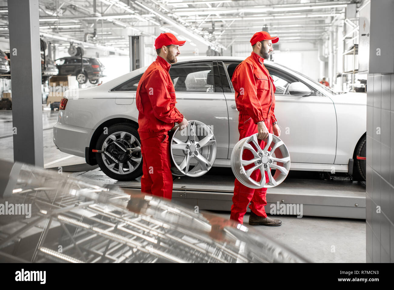 Two male auto mechanics in red uniform walking with alloyed wheels at ...