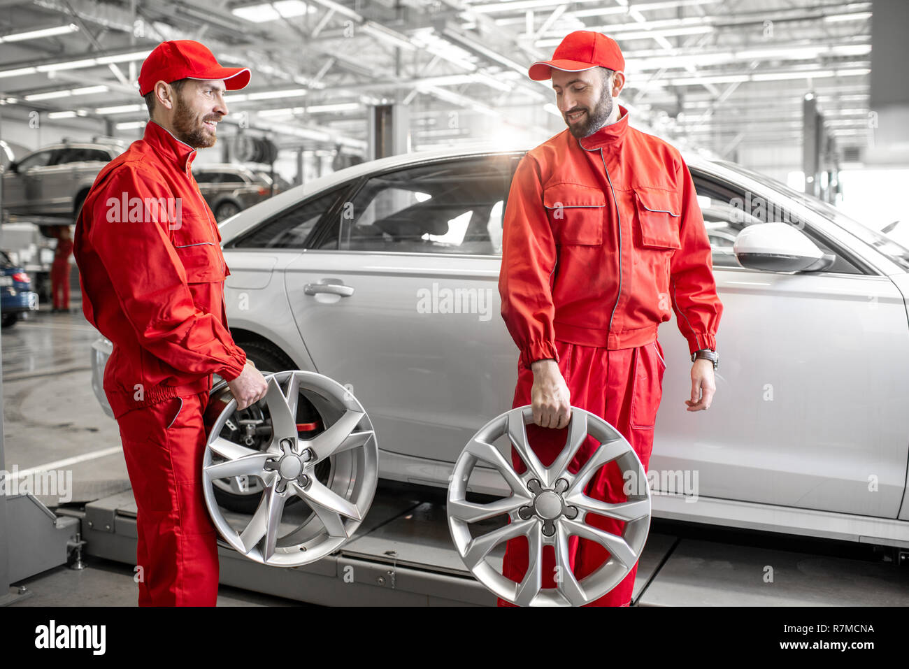 Two male auto mechanics in red uniform walking with alloyed wheels at ...