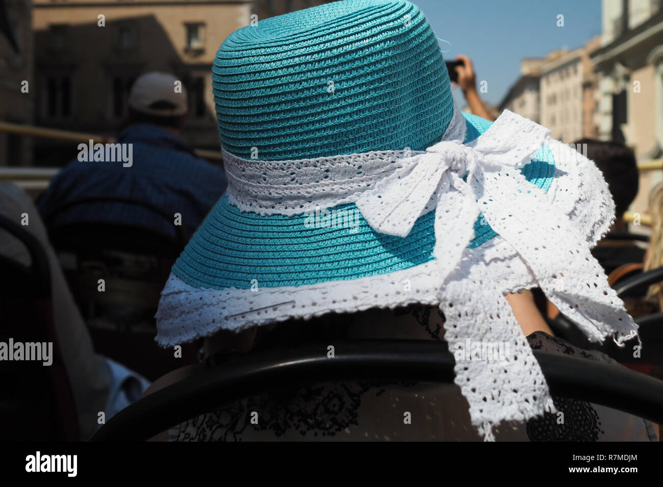 Tourist on open top bus wearing a turquoise straw hat with lacy bow ...