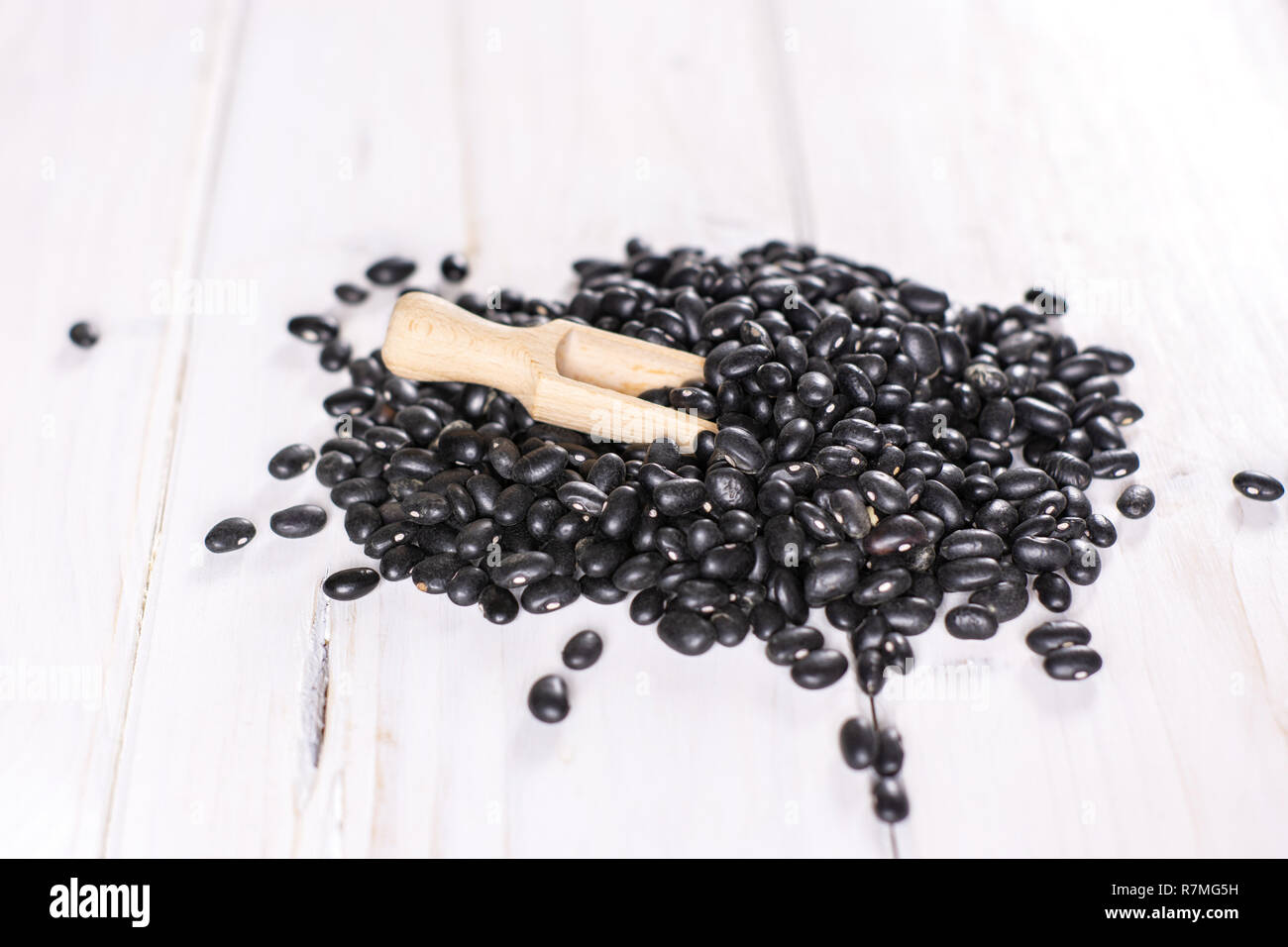 Lot of whole raw black turtle beans with wooden scoop on white wood ...