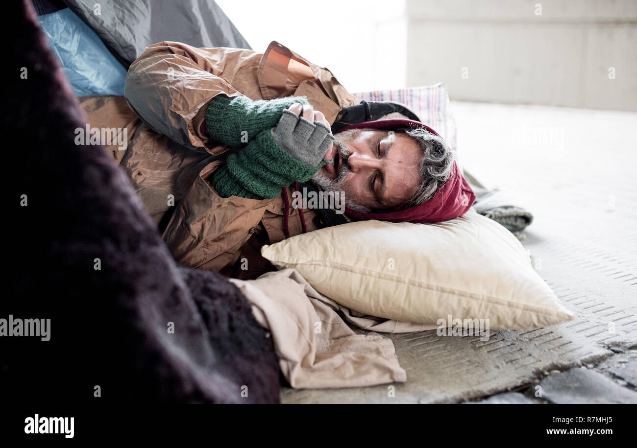 Homeless beggar man lying on the ground outdoors in city, warming up ...