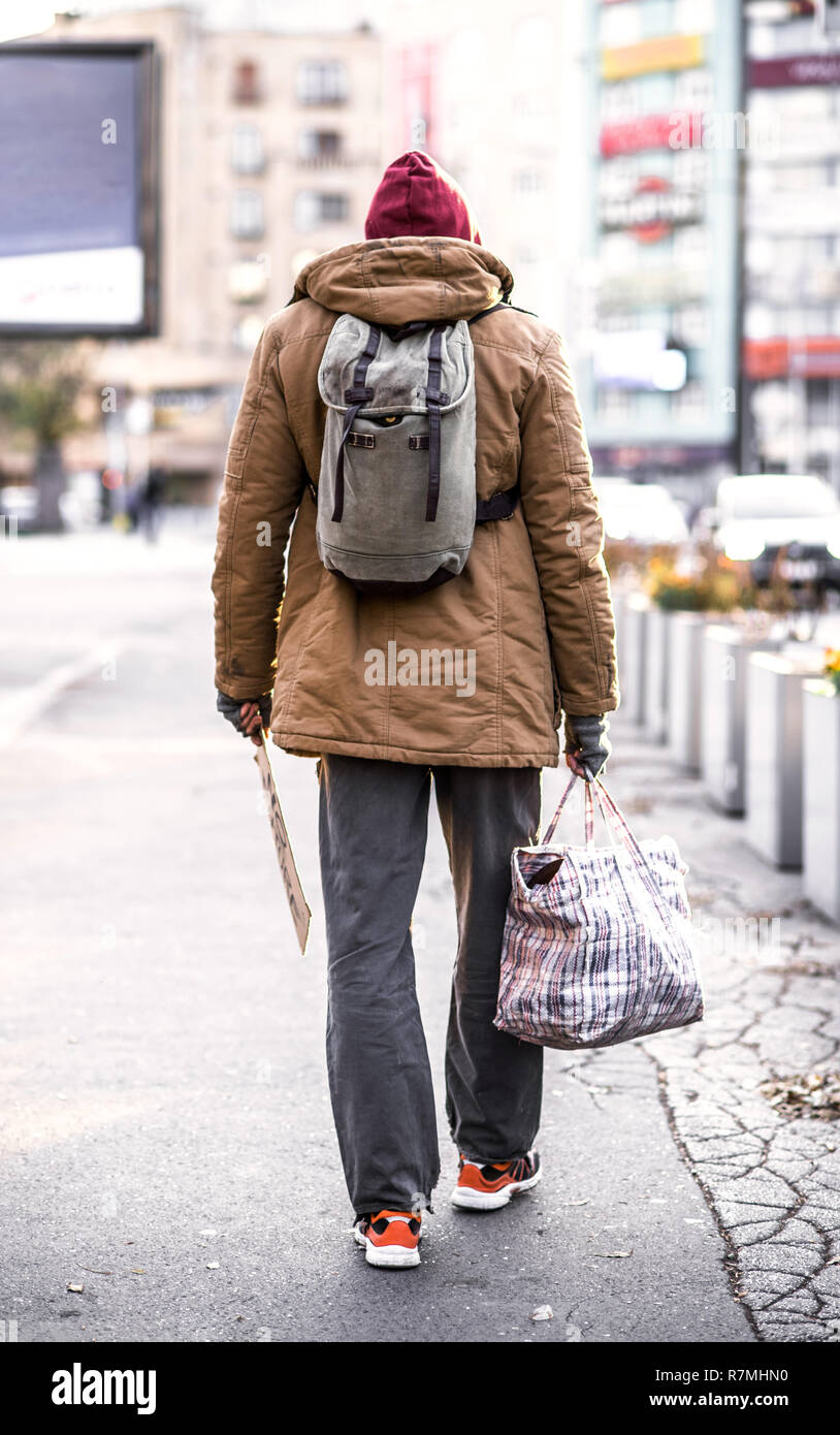 A rear view of homeless beggar man walking outdoors in city, holding ...