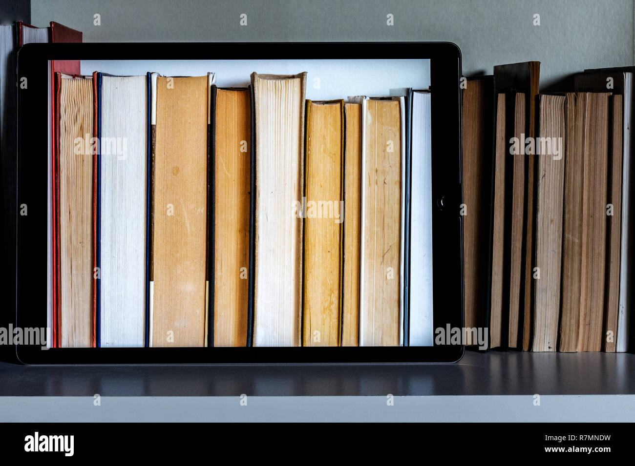 Tablet and books on a bookshelf. The bright screen shows the books ...
