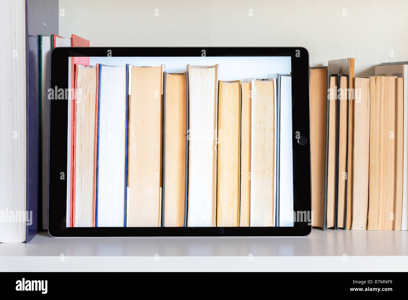 Tablet and books on a bookshelf. The screen shows the books behind ...
