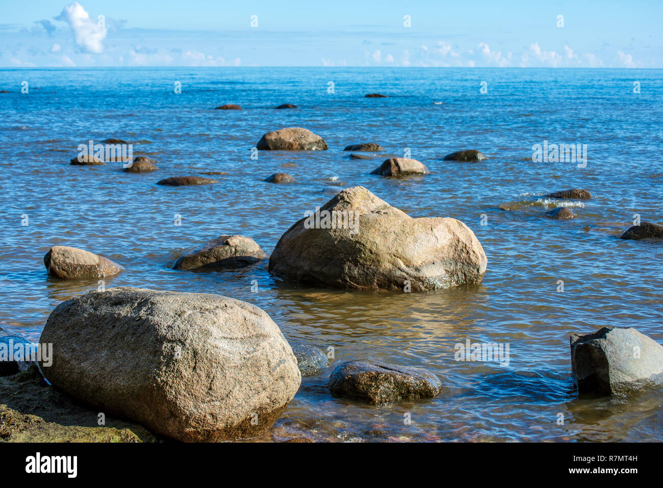rock covered beach in countryside in Latvia, large rocks in water with ...