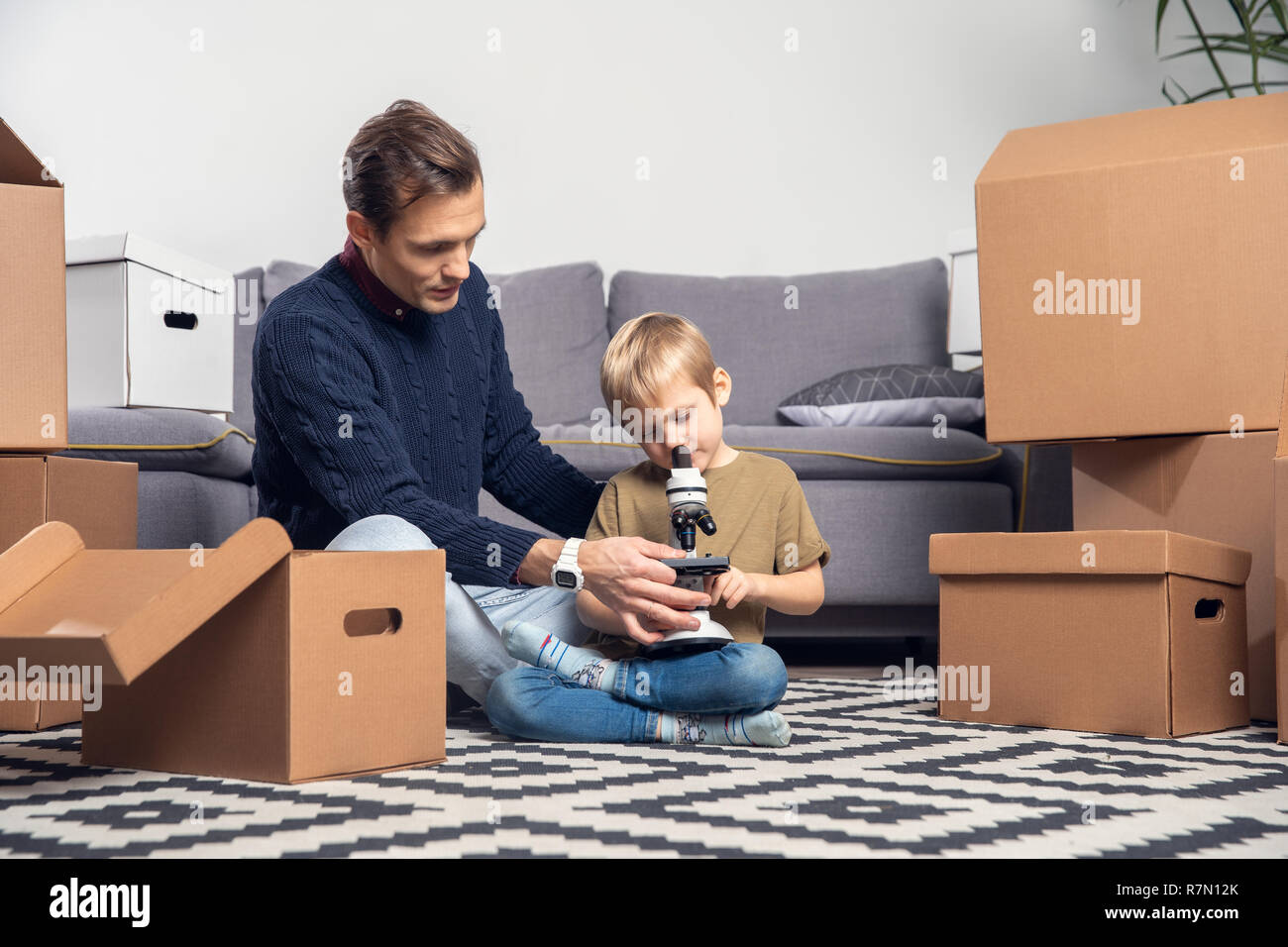Image of man and small boy with microscope sitting on floor among ...