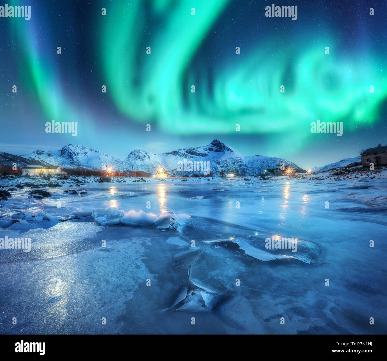 Northern lights above snowy mountains, frozen sea coast and houses in ...