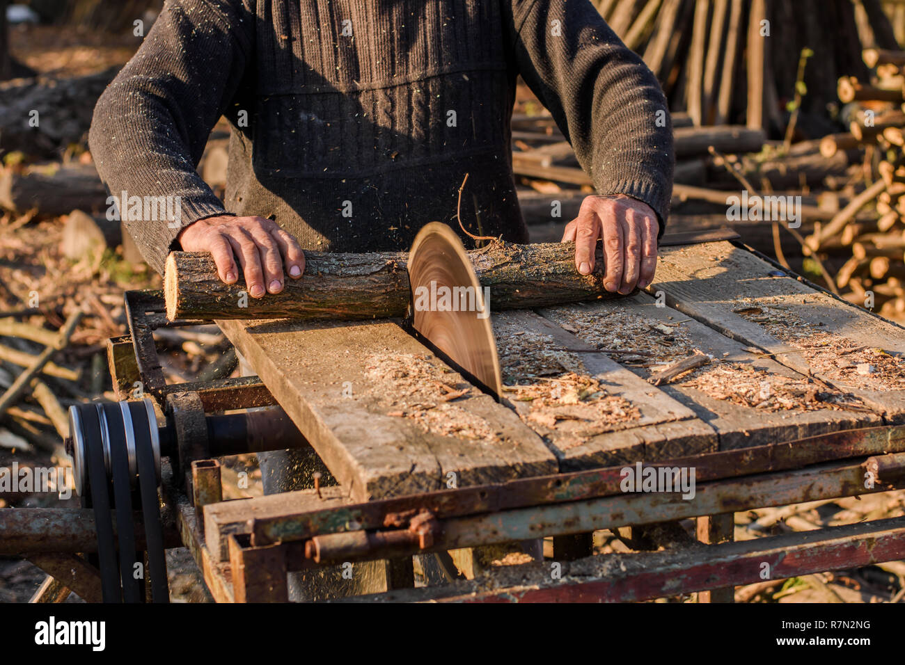Man cutting wood using stationary circular saw outdoors in the sun ...