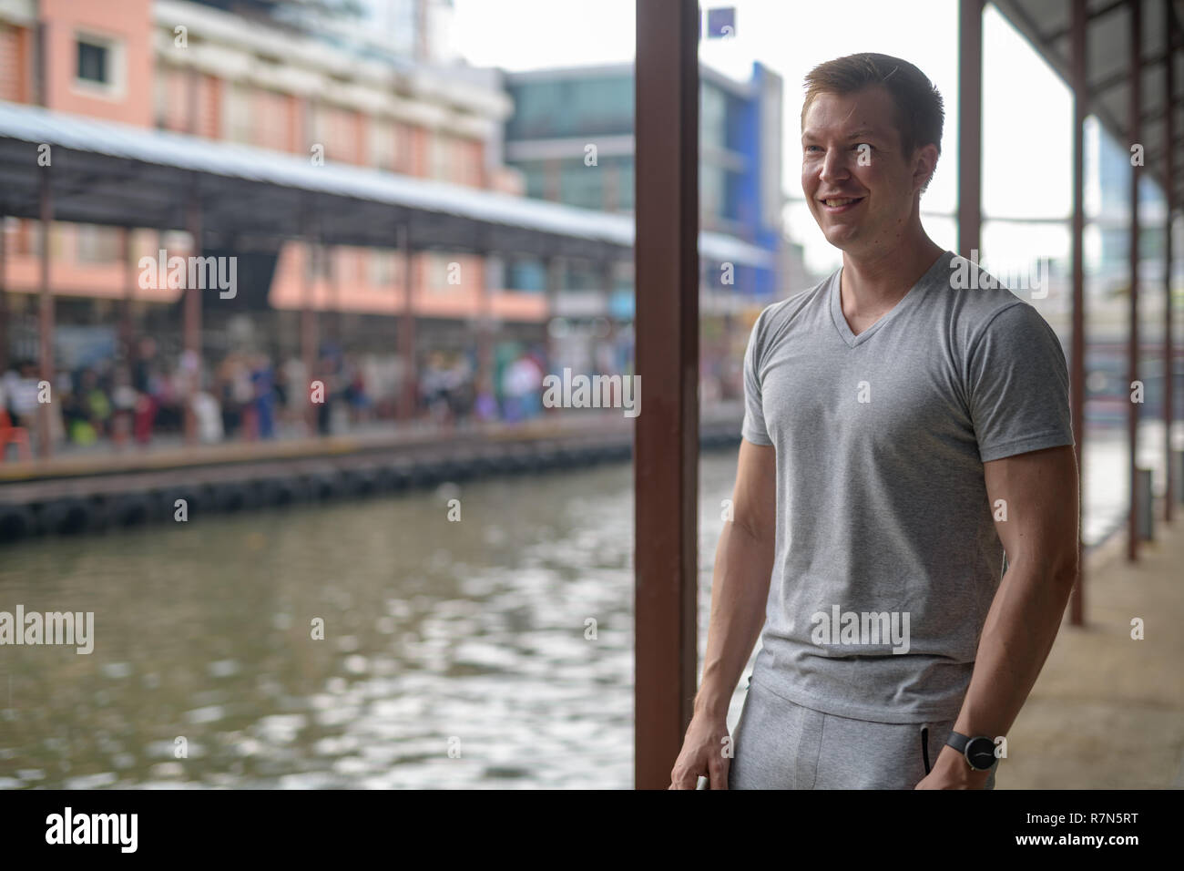 Young happy tourist man thinking while waiting at the local pier in ...