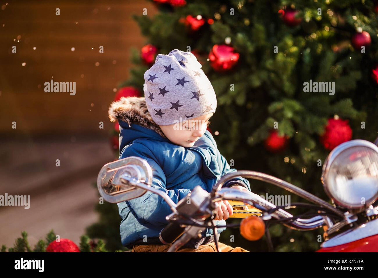 Cute little baby boy on the red motorcycle. Christmas tree and new year ...
