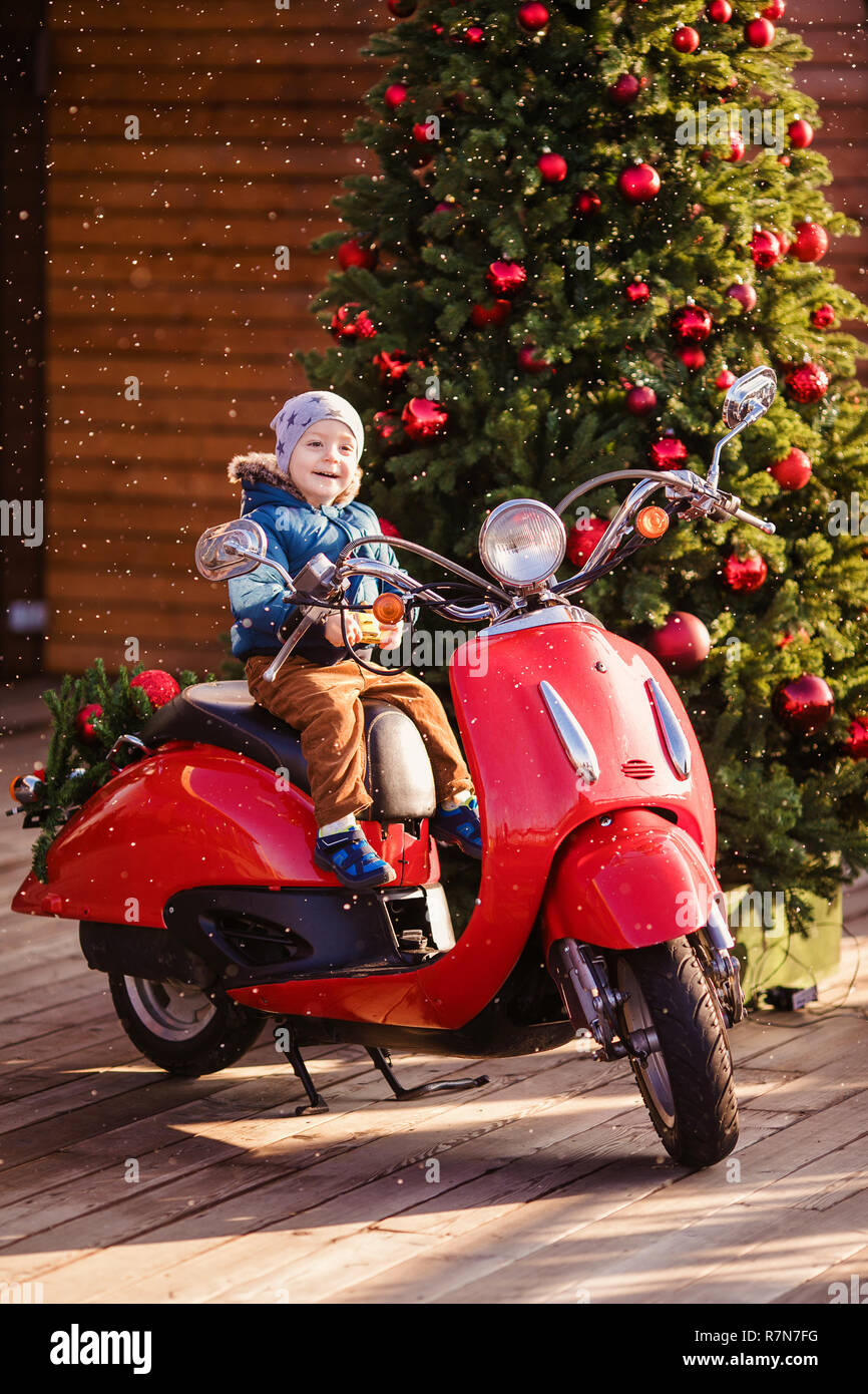 Cute little baby boy on the red motorcycle. Christmas tree and new year ...