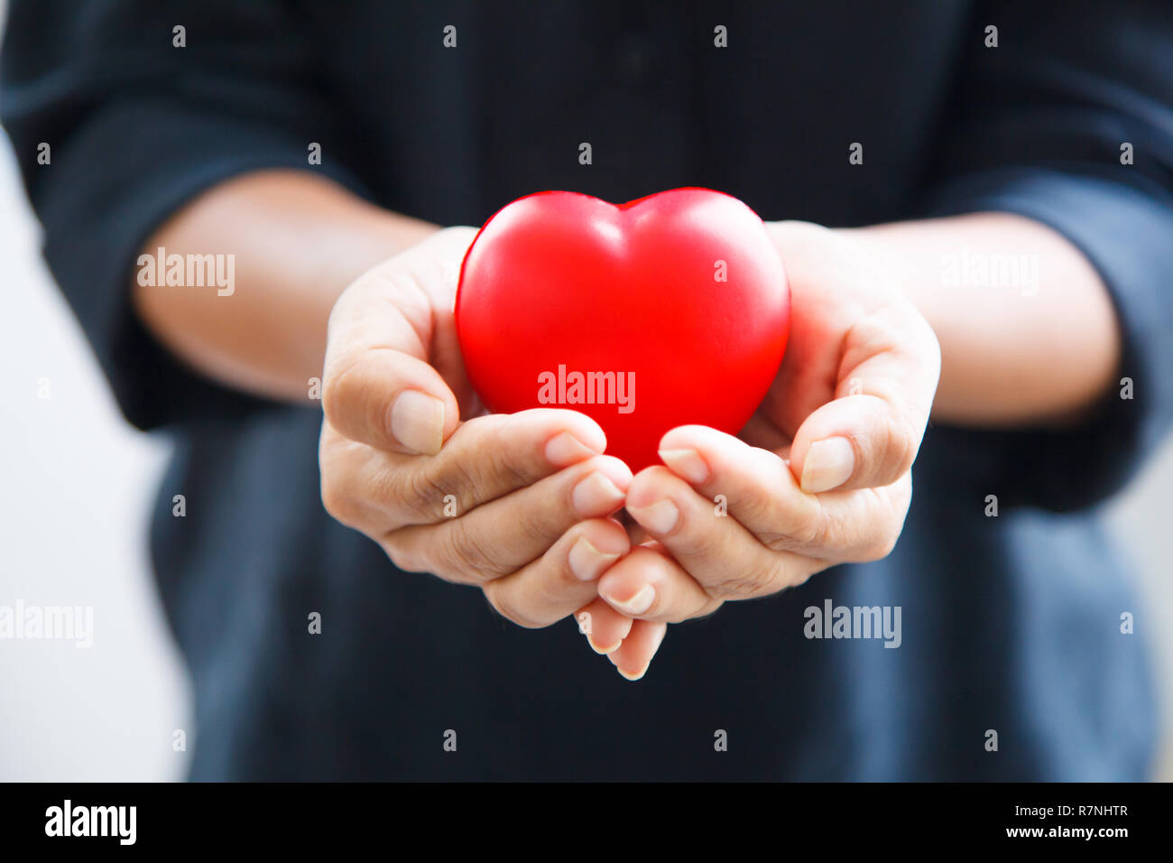 red heart in female's both hands in black suit background, represents ...