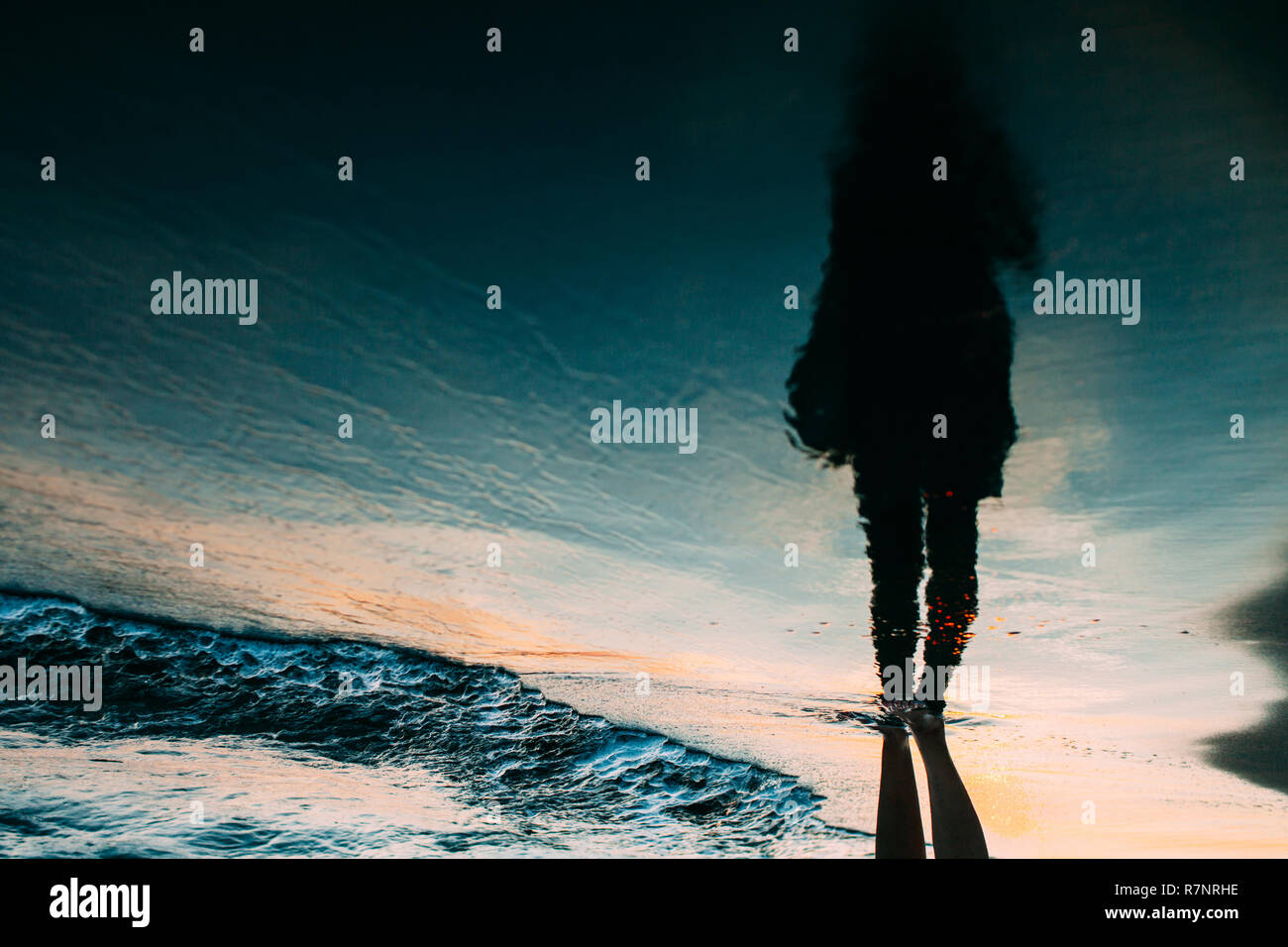 Reflection silhouette of a young woman at the seashore with sunset ...