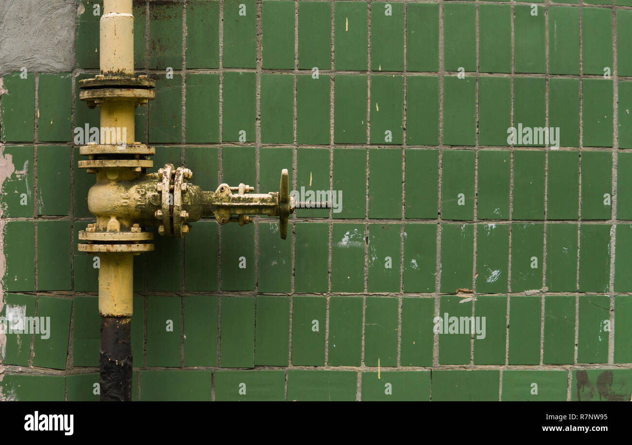 Old weathered gas crane and pipe on the background of a green wall. Old ...