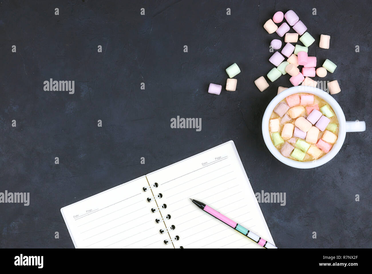 Cup with coffee and marshmallows, blank open notebook with pen on black ...