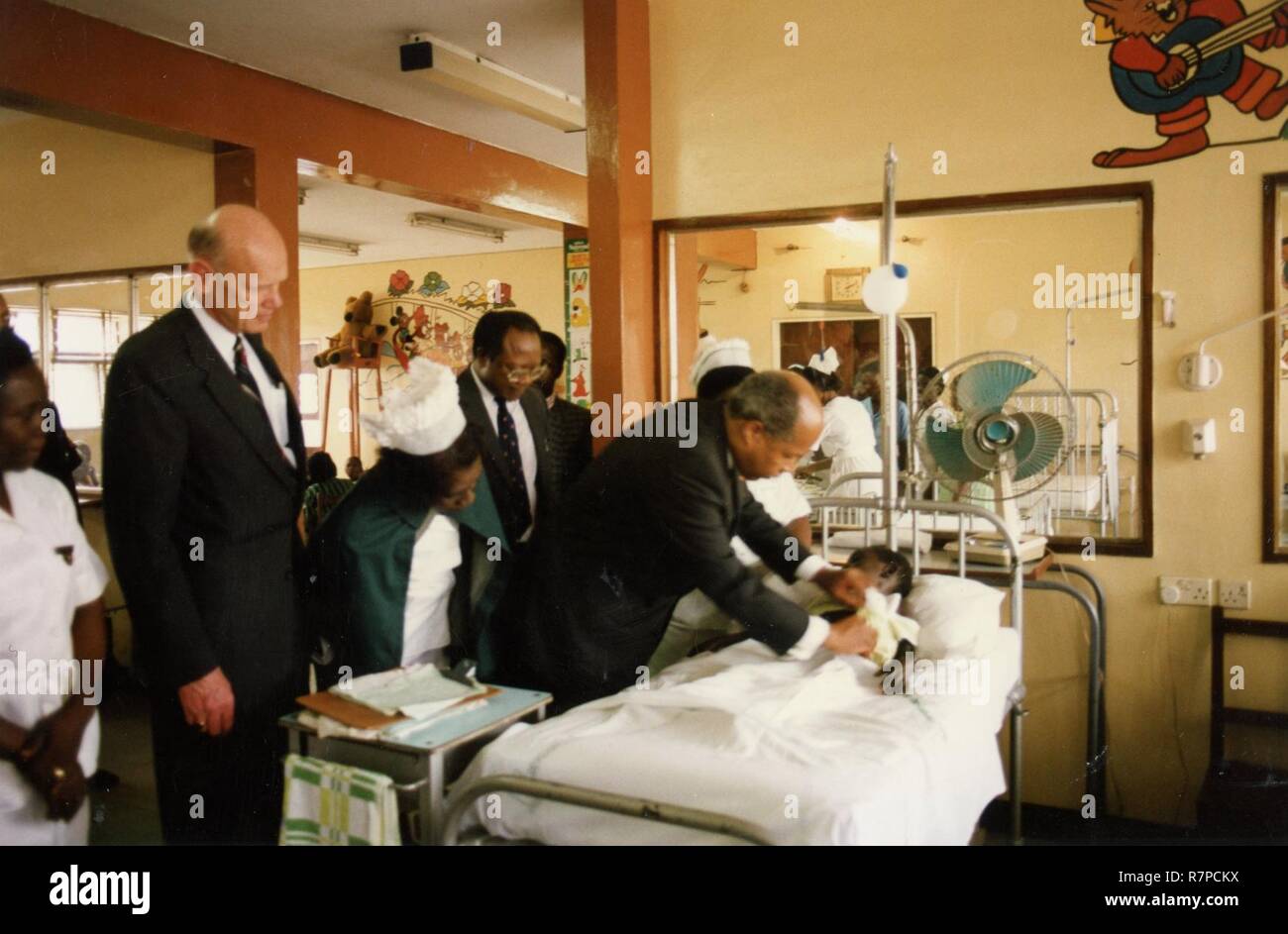 A GROUP MEN AND WOMEN AT THE HOSPITAL WITH A PATIENT IN THE BED BEING ...