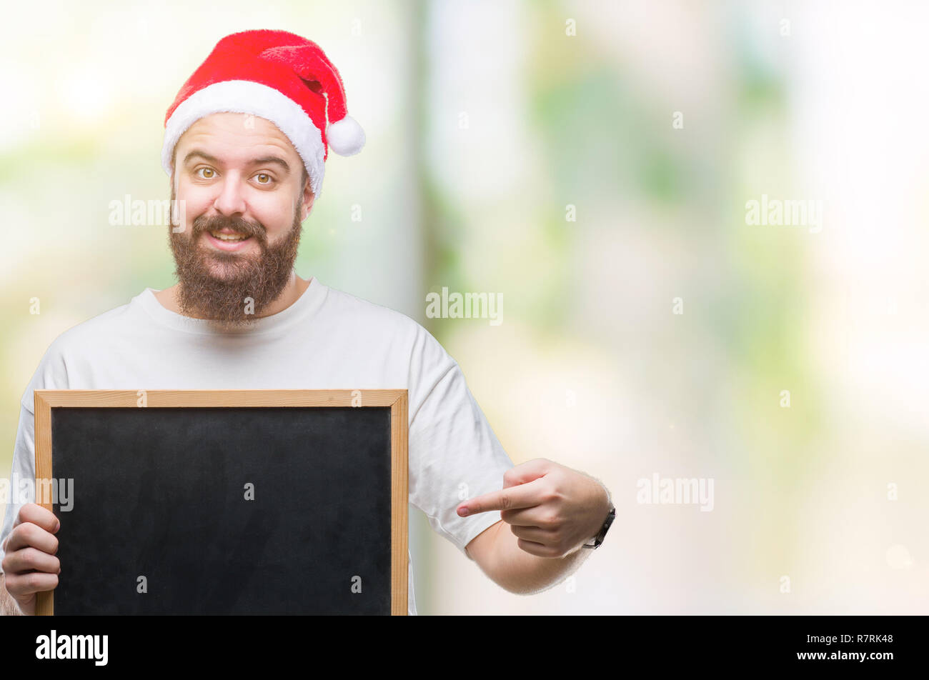 Young caucasian hipster man wearing christmas hat holding blackboard ...