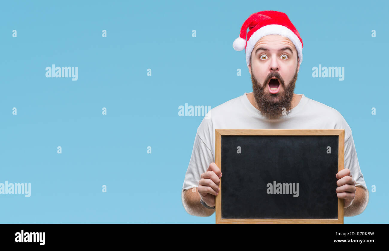 Young caucasian hipster man wearing christmas hat holding blackboard ...