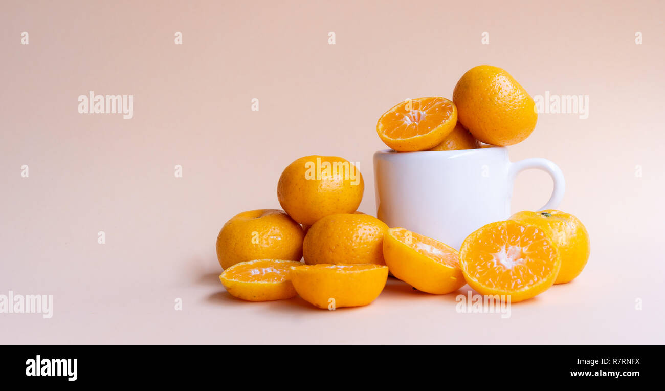 whole and half cut fresh oranges with white ceramic mug on soft cream ...
