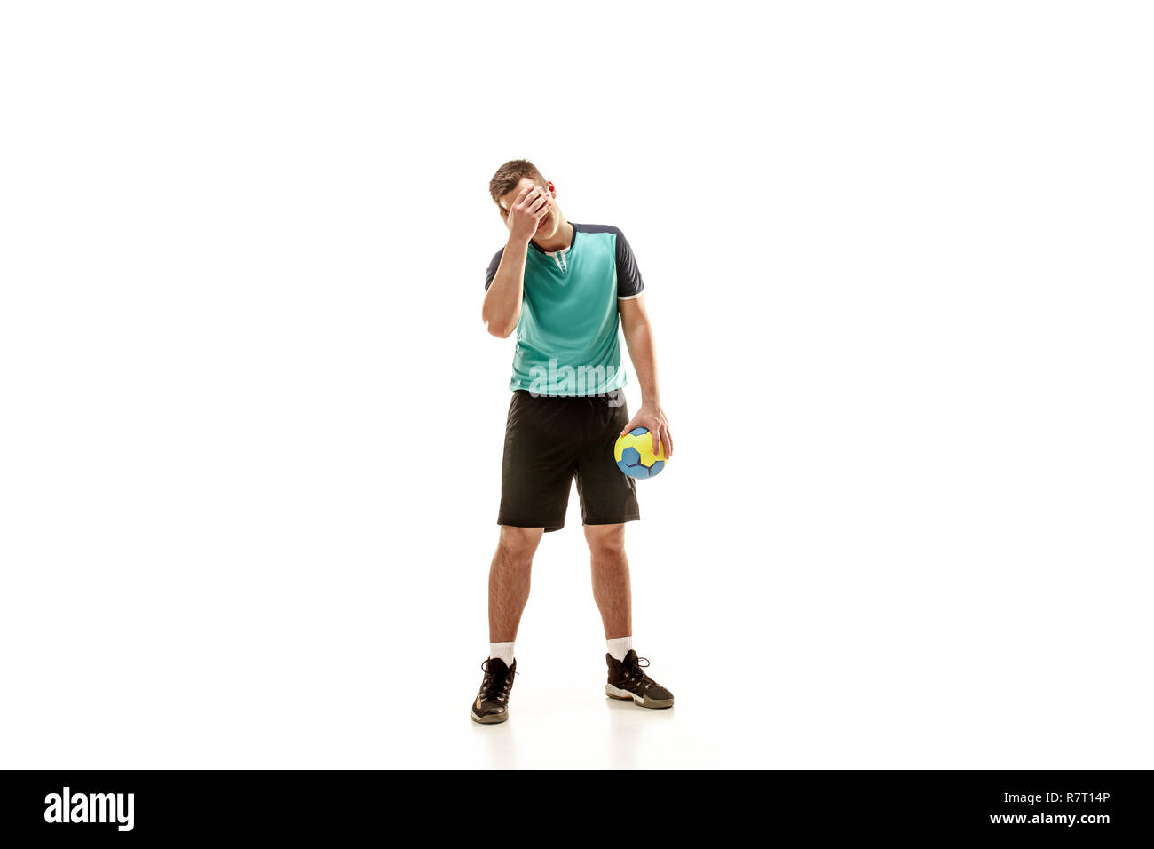 The sad fit caucasian young male handball player at studio on white ...