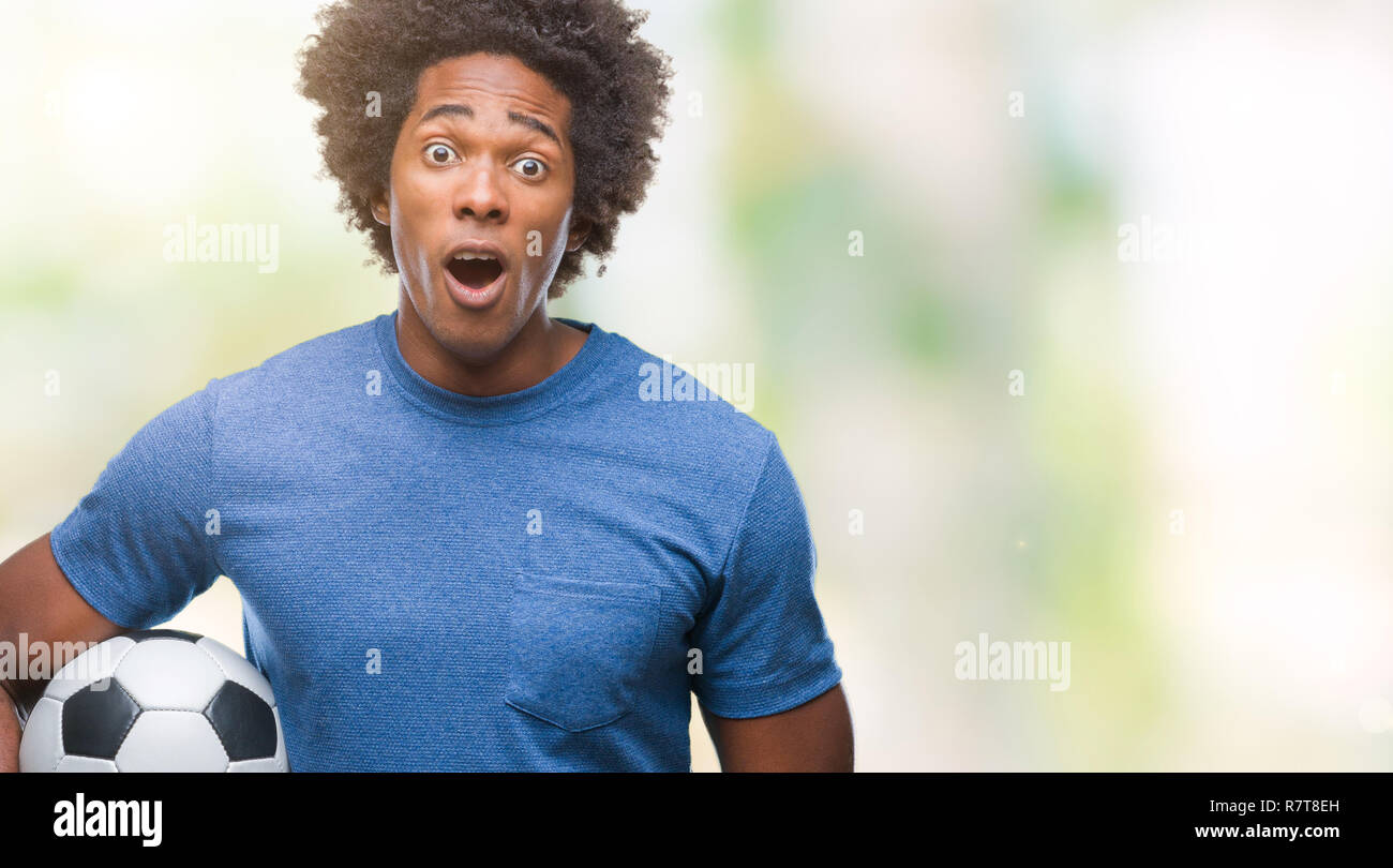 Afro american man holding football ball over isolated background scared ...
