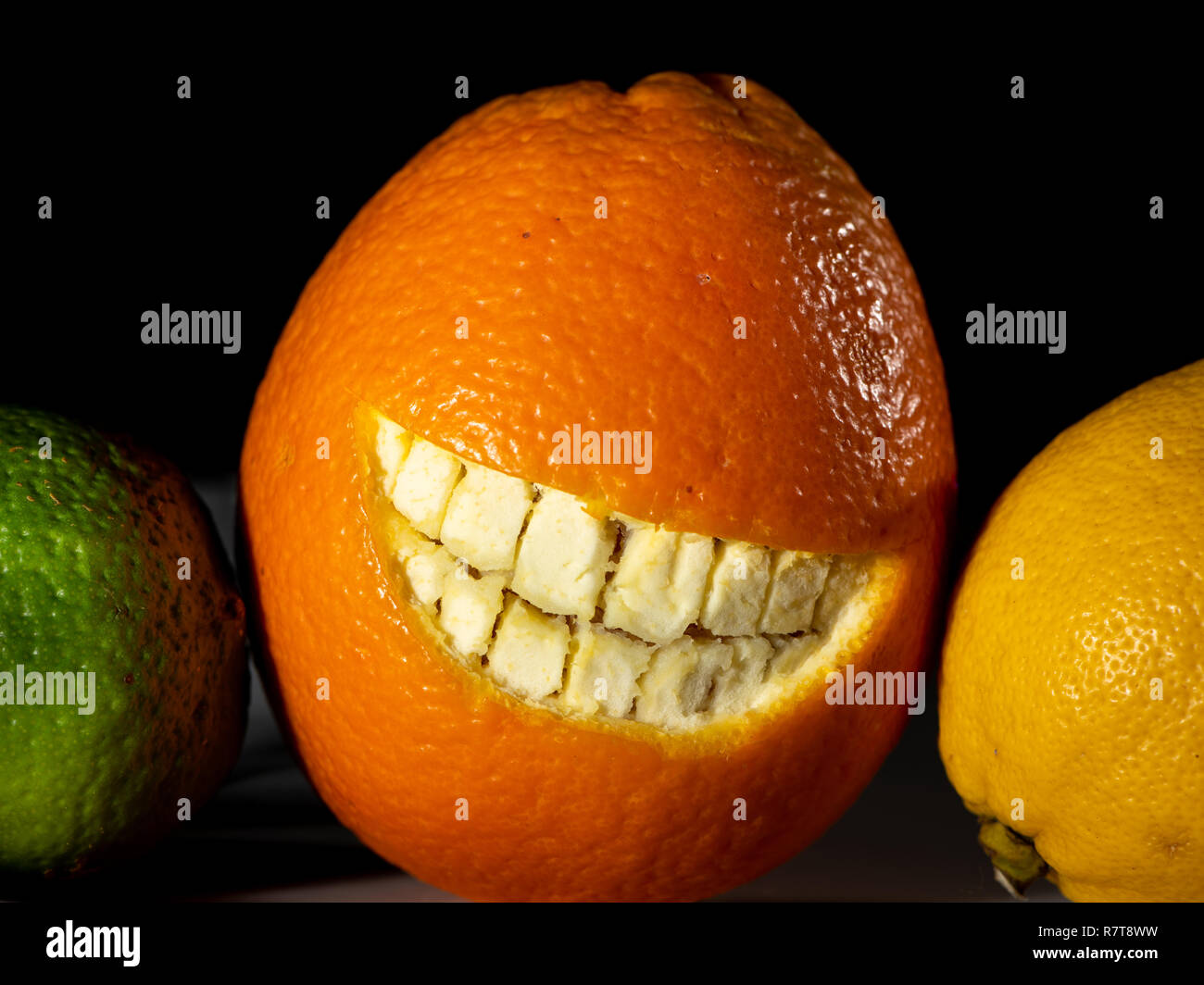 Orange with a cut smile in the skin, lemon and lime, black background ...