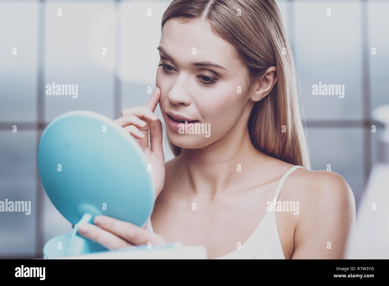 Beautiful young woman looking at her face Stock Photo - Alamy