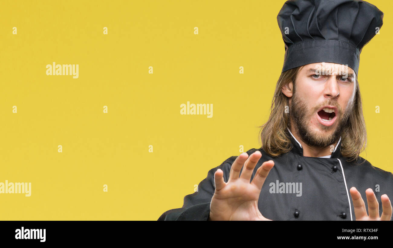 Young handsome cook man with long hair over isolated background afraid ...