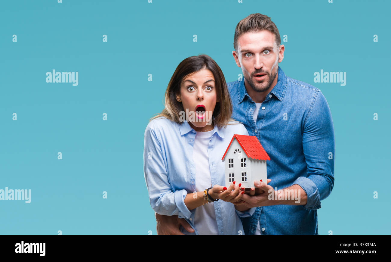 Young couple in love holding house over isolated background scared in ...