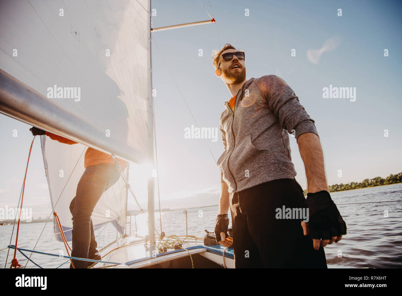 Low angle shot of a young man sailor wearing sunglasses and gloves on a ...