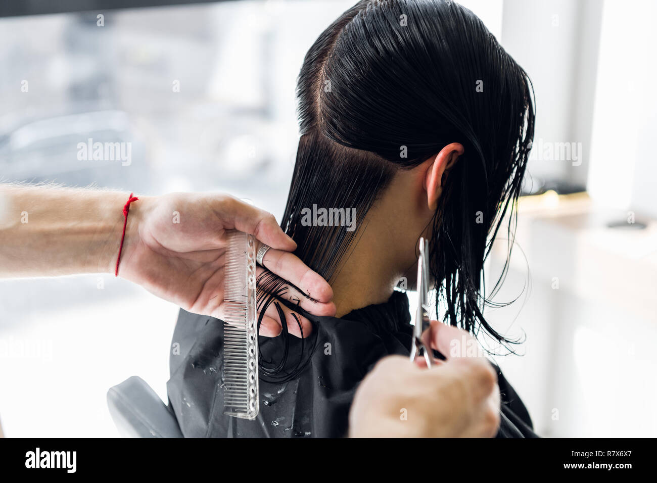 Man's hands cut and comb female dark brown hair in a beauty salon with ...