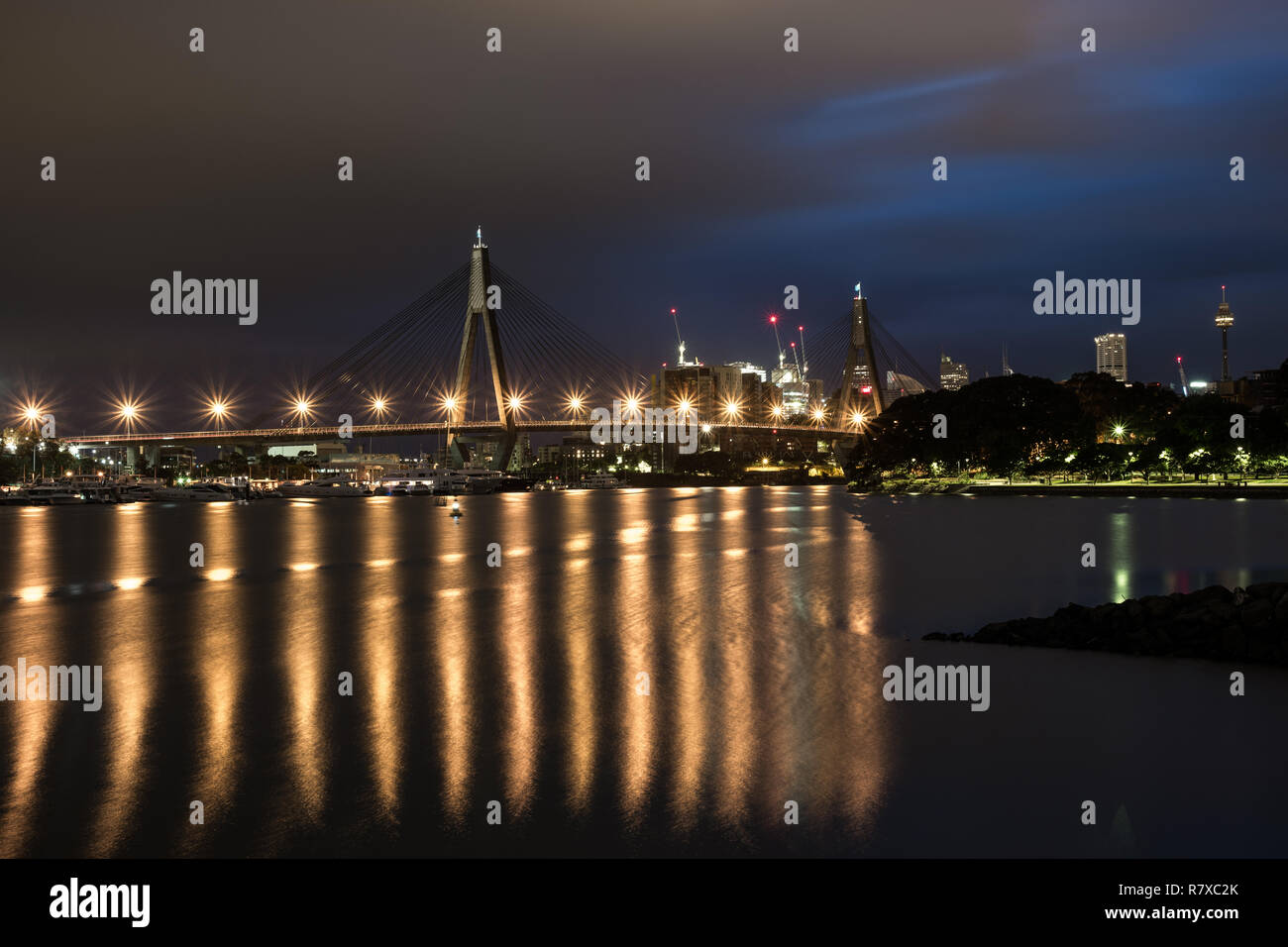 Bridge at night with lights reflecting on water and city in background ...