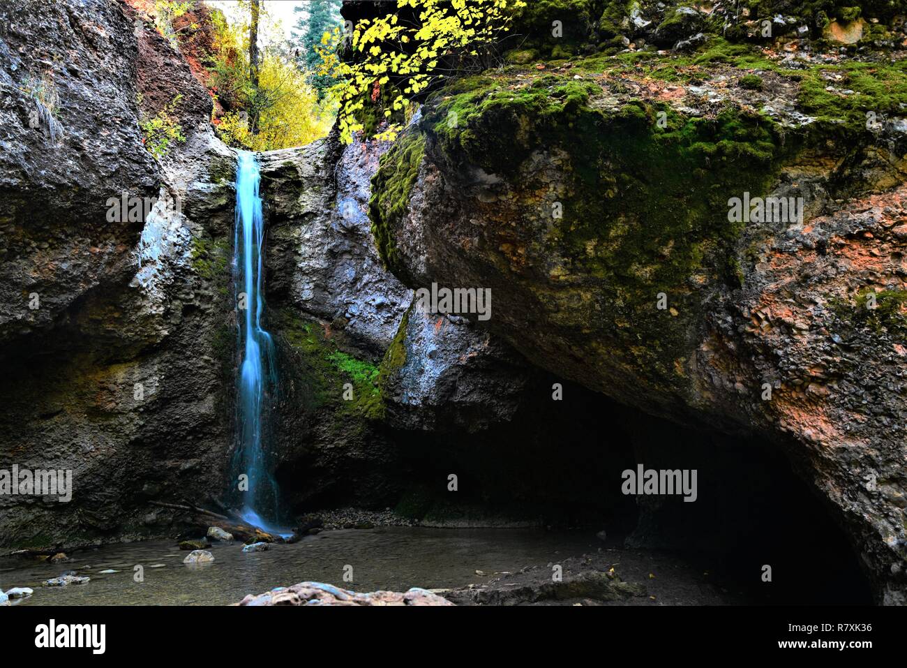 Hidden grotto with small waterfall and autumn colors in background ...