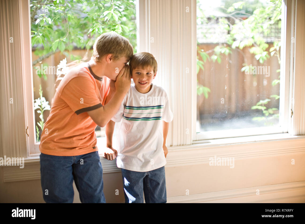 Boy whispering into the ear of his younger brother inside their house ...