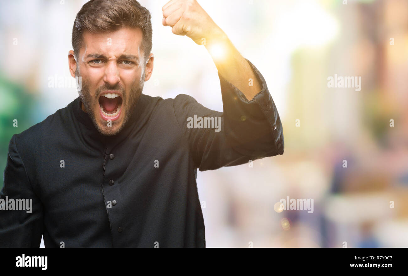 Young catholic christian priest man over isolated background angry and ...