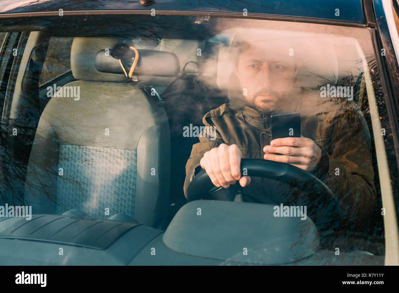 Front view of man driving car and texting on mobile phone which is ...