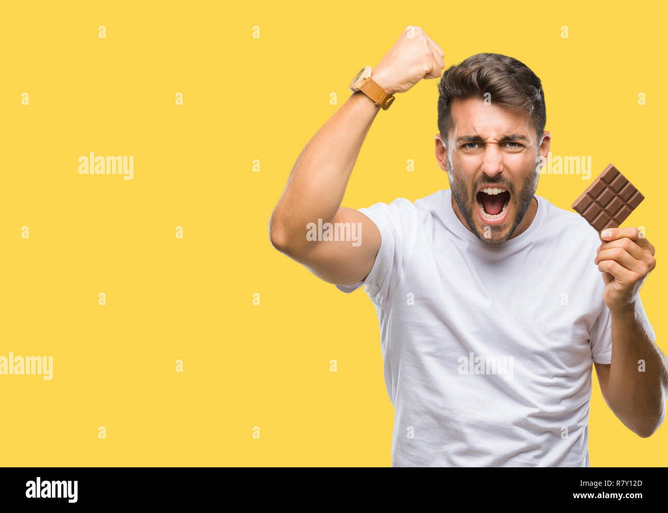 Young handsome man eating chocolate bar over isolated background ...