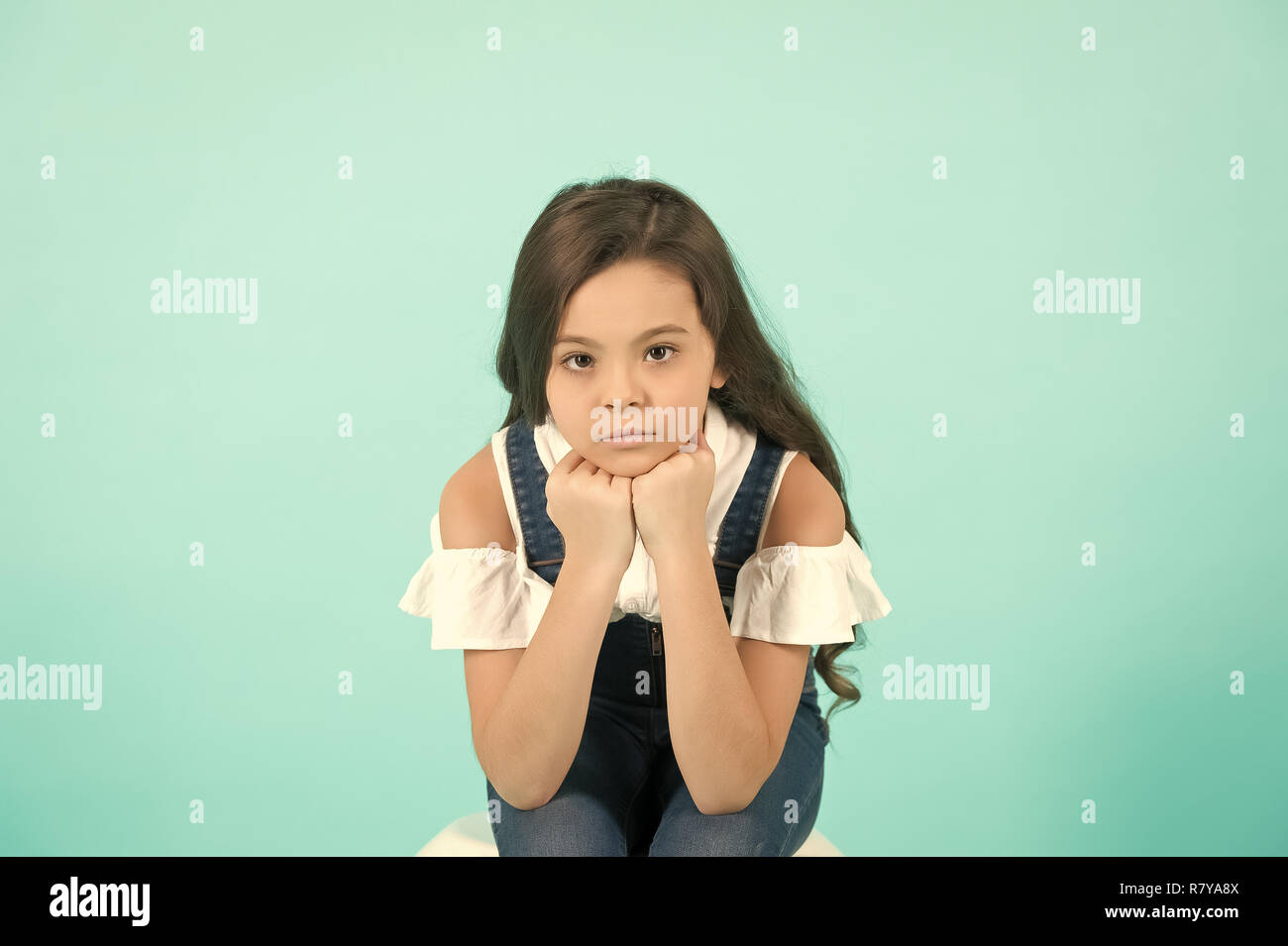 Child prop chin on hands on blue background. Girl with long brunette ...
