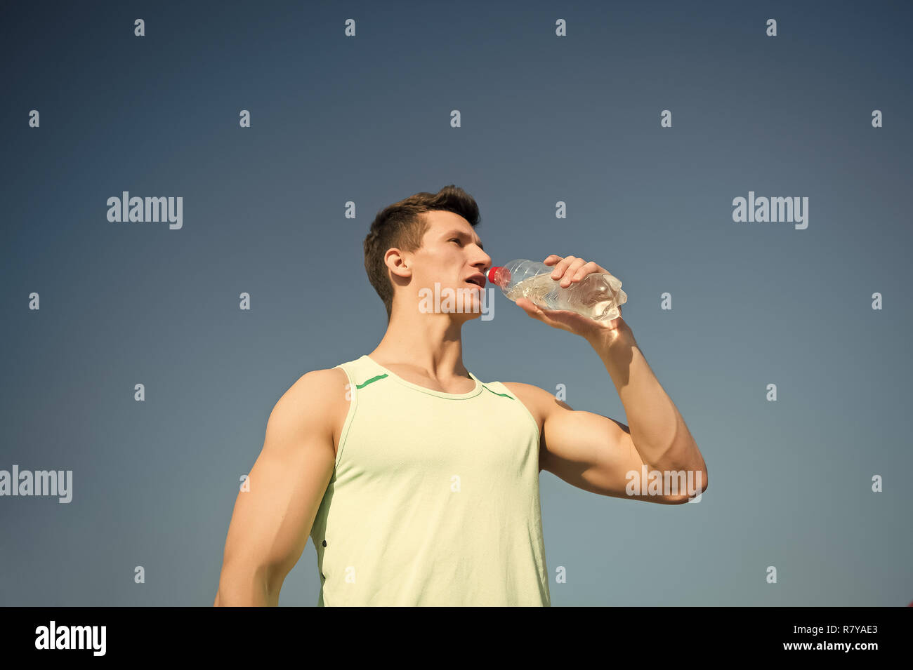 Man drinking water from bottle on sunny day. Athlete in green tshirt on ...