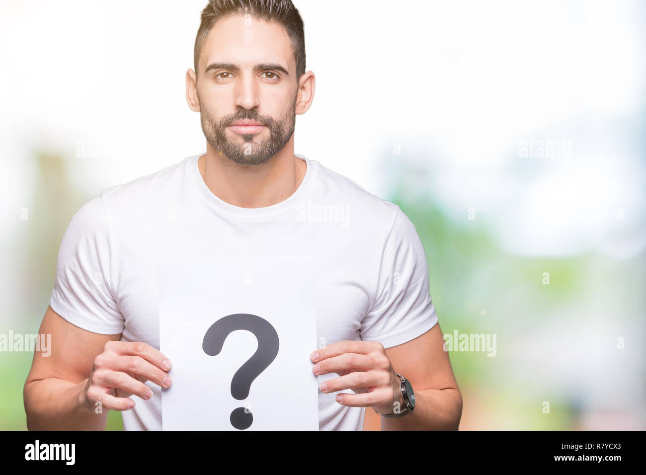 Handsome young man holding paper with question mark over isolated ...
