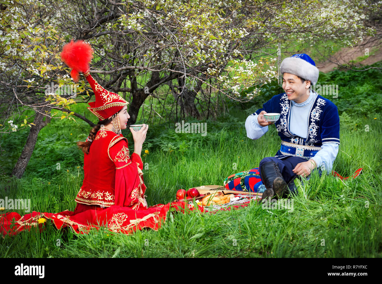 Kazakh couple drinking tea on the green grass in apple garden of Almaty ...