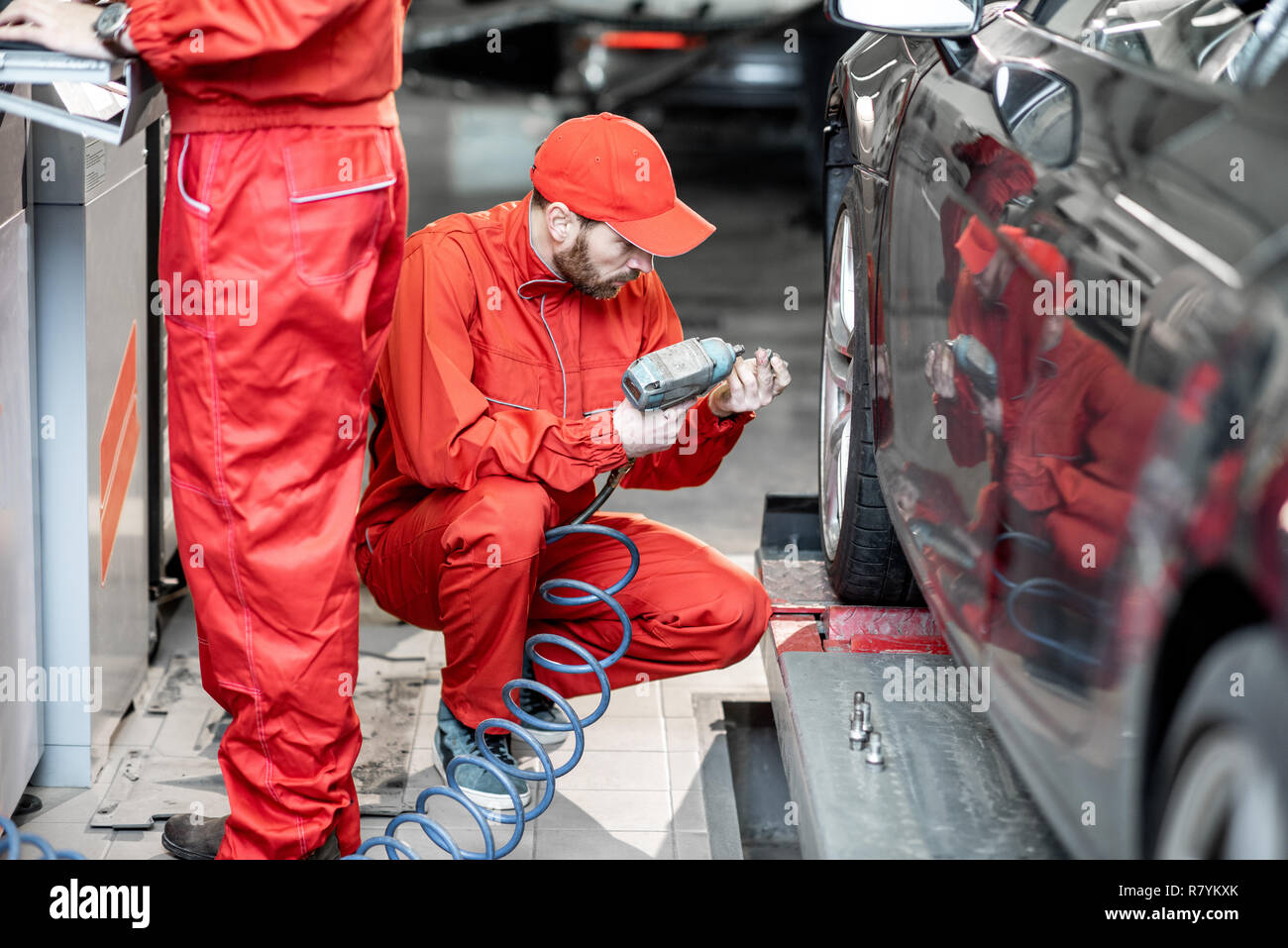 Two car service workers in red uniform changing wheel of a sport car at ...