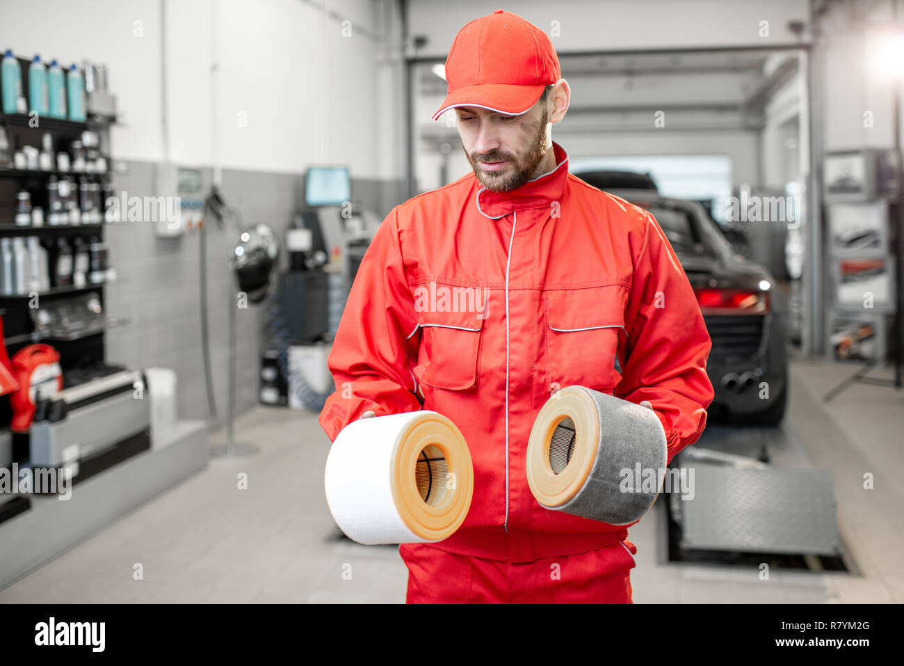 Auto mechanic in red uniform holding new and used air filter standing ...