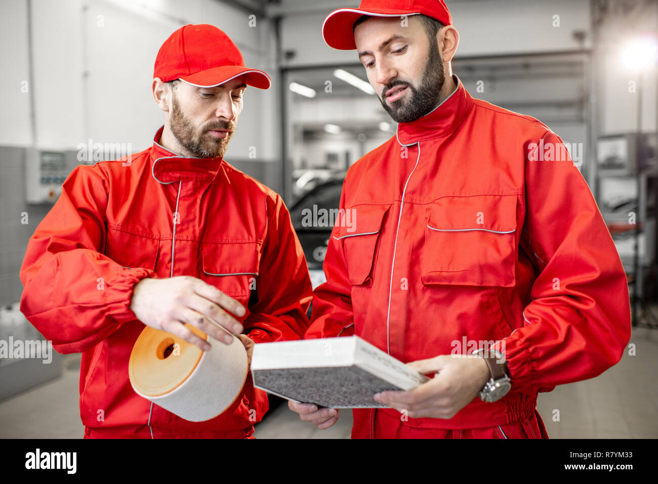 Auto mechanic in red uniform holding new and used air filter standing ...