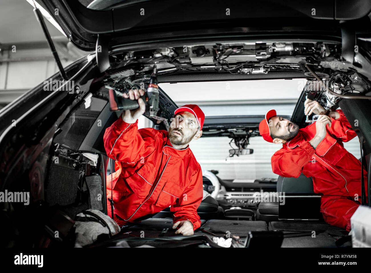 Two auto service workers in red uniform disassembling new car interior ...