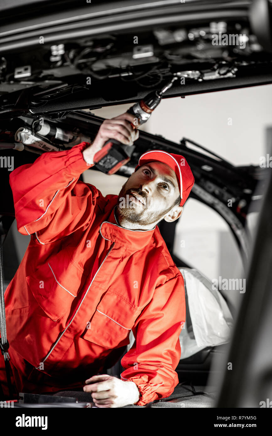 Handsome auto service worker in red uniform disassembling new car ...