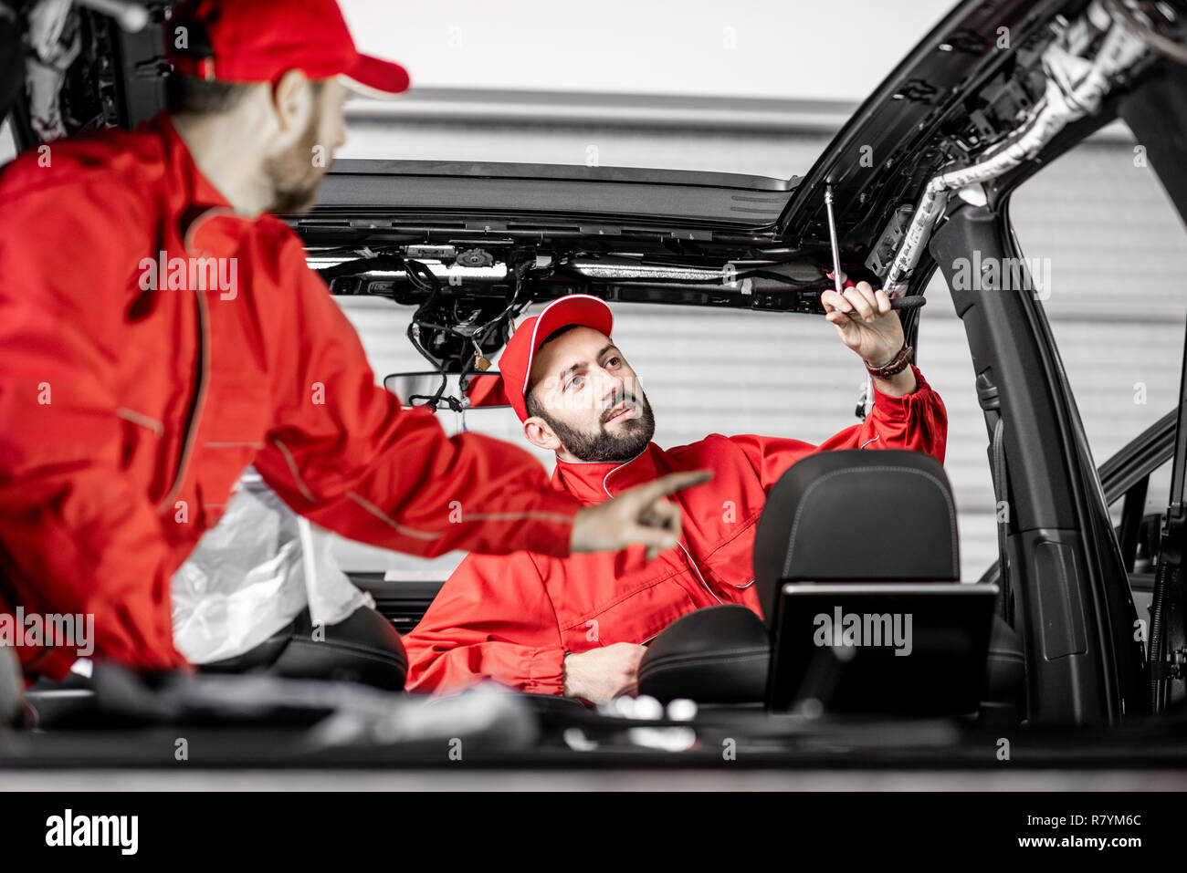 Two auto service workers in red uniform disassembling new car interior ...